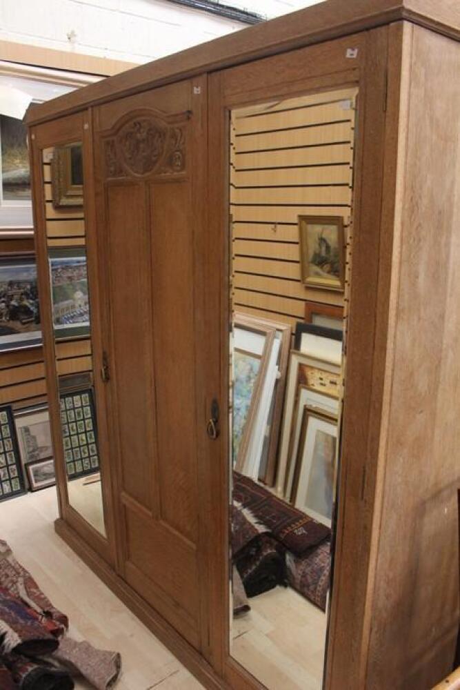 An Arts and Crafts oak triple sectioned wardrobe, mirrored doors to ...