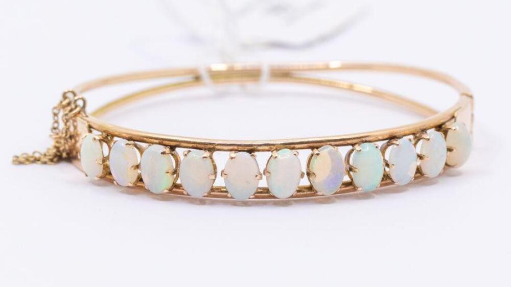 An opal and 14ct rose gold bangle, comprising a row of eleven claw set ...