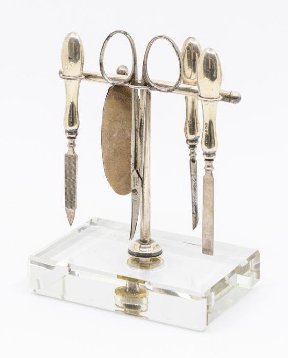 A novelty George V silver manicure set on glass base, to include; nail ...
