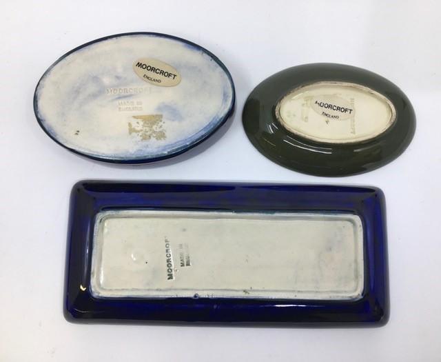 A collection of two Moorcroft trays together with a Moorcroft lidded box.