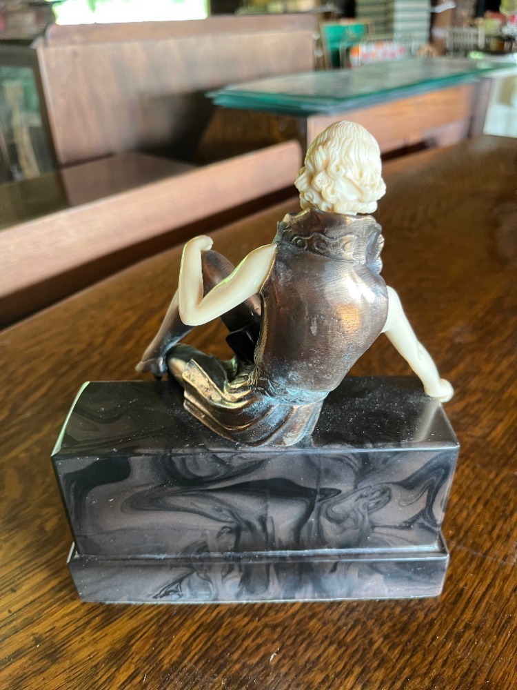 Art Deco style lady figure sitting on plinth.